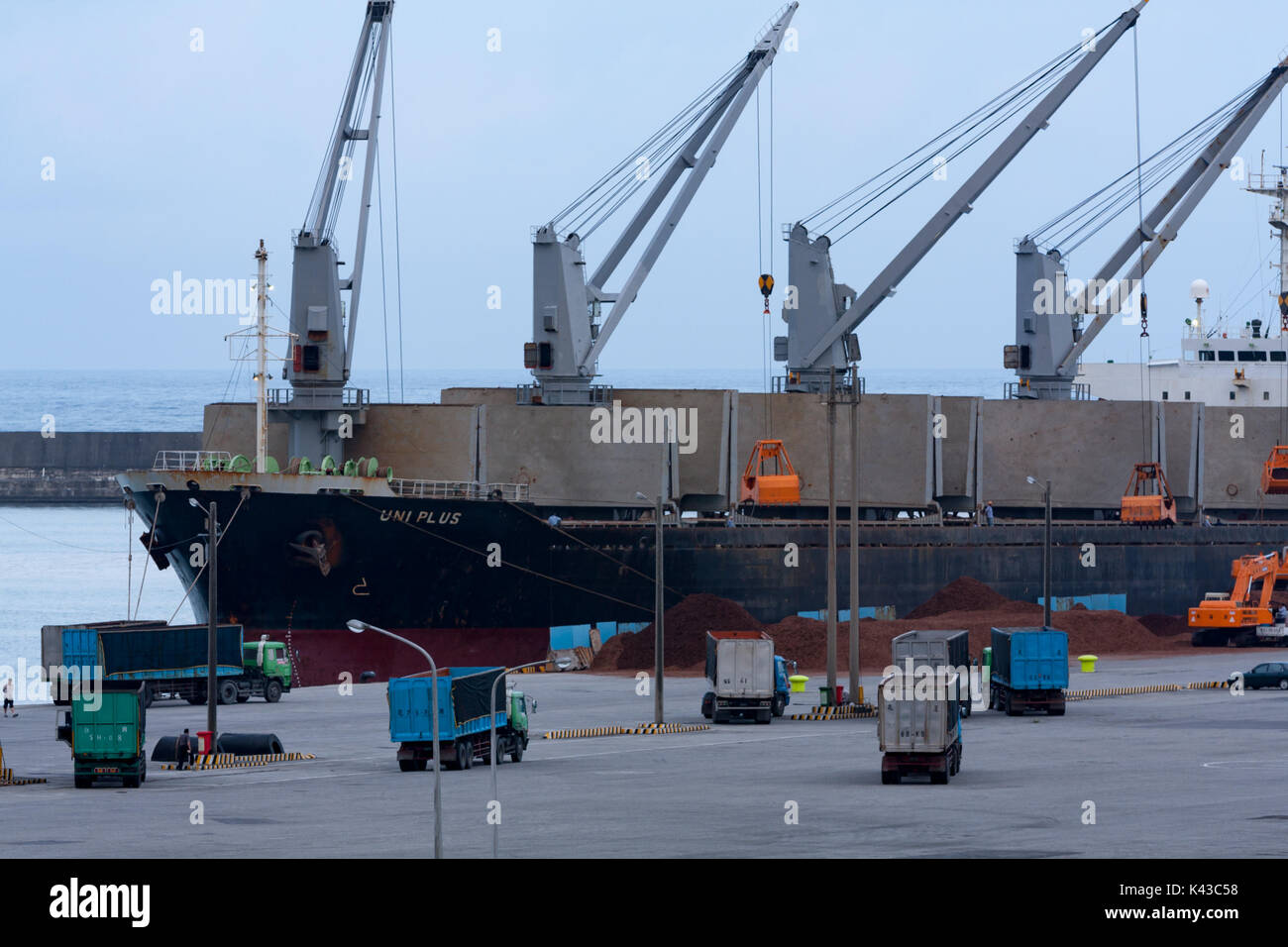 Uniplus bulk carrier cranes unloading loads with dump trucks waiting ...