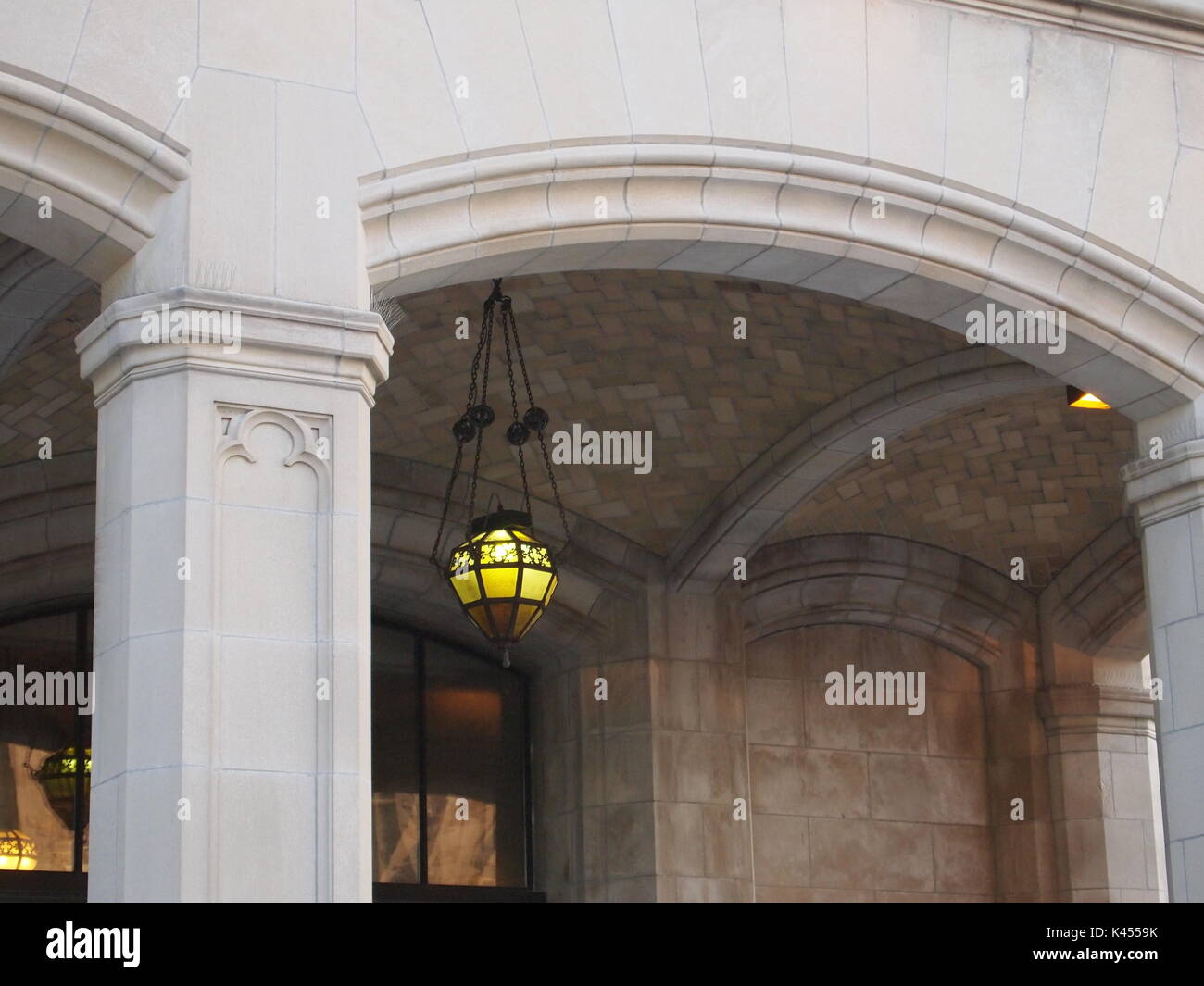 Detail of a stone arch and column, lit by a yellow glass hanging ...