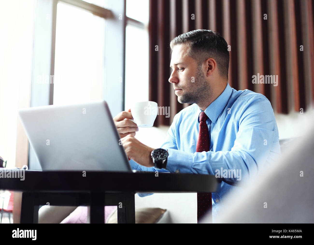Smiling young handsome businessman holding cup of coffee and working ...