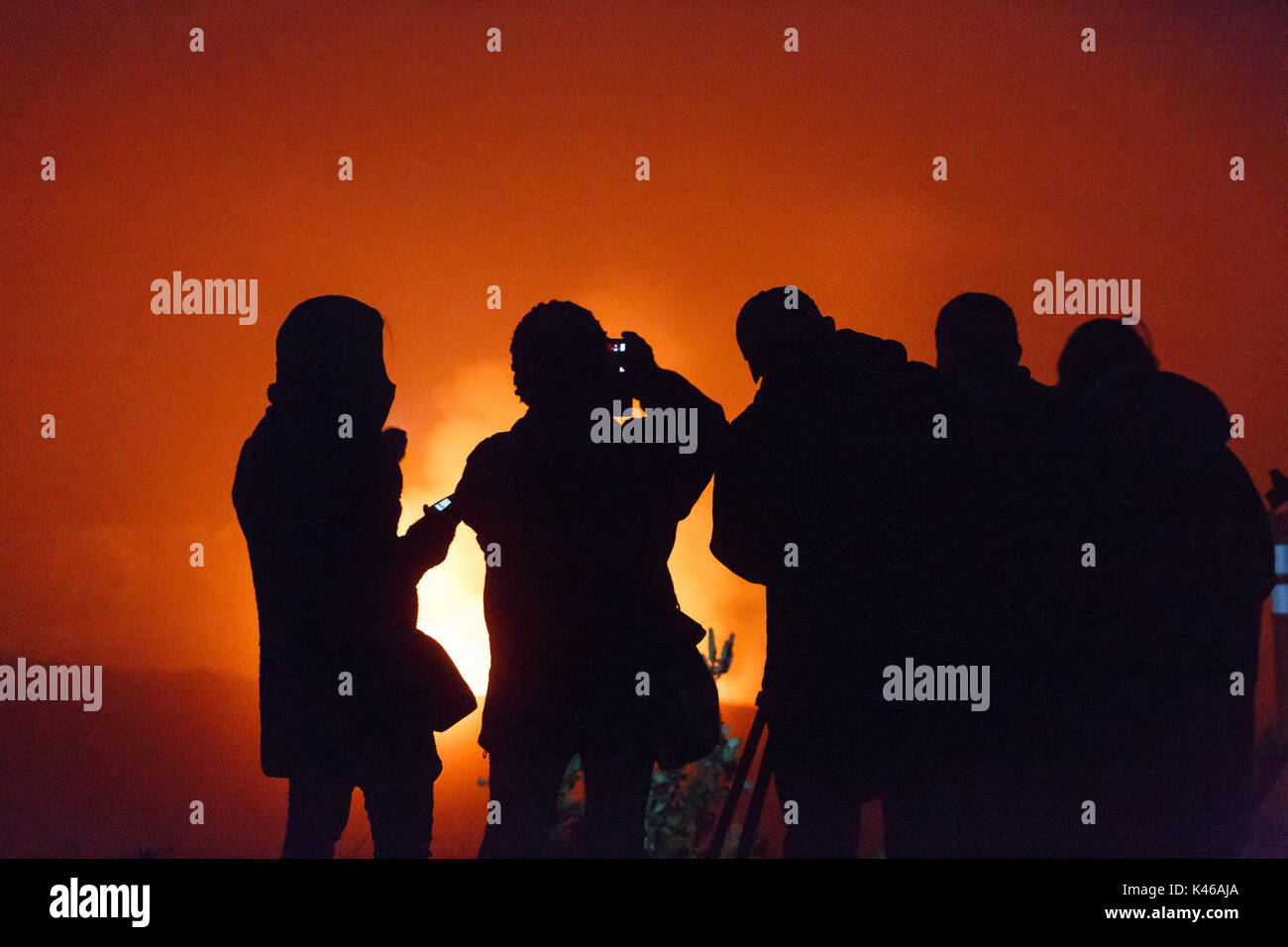 Group of people stand on the rim of an active volcano glowing in the ...