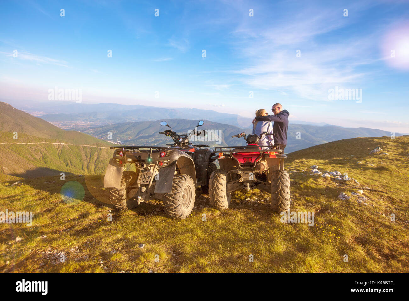 Rear view of young pair near atv. Man is showing something in distance ...