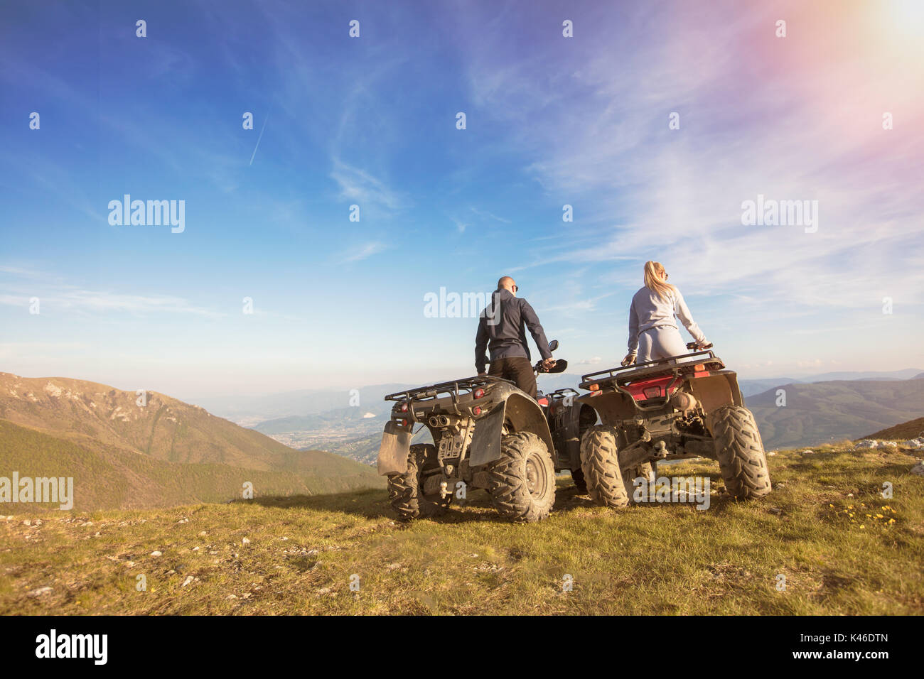 Rear view of young pair near atv. Man is showing something in distance ...