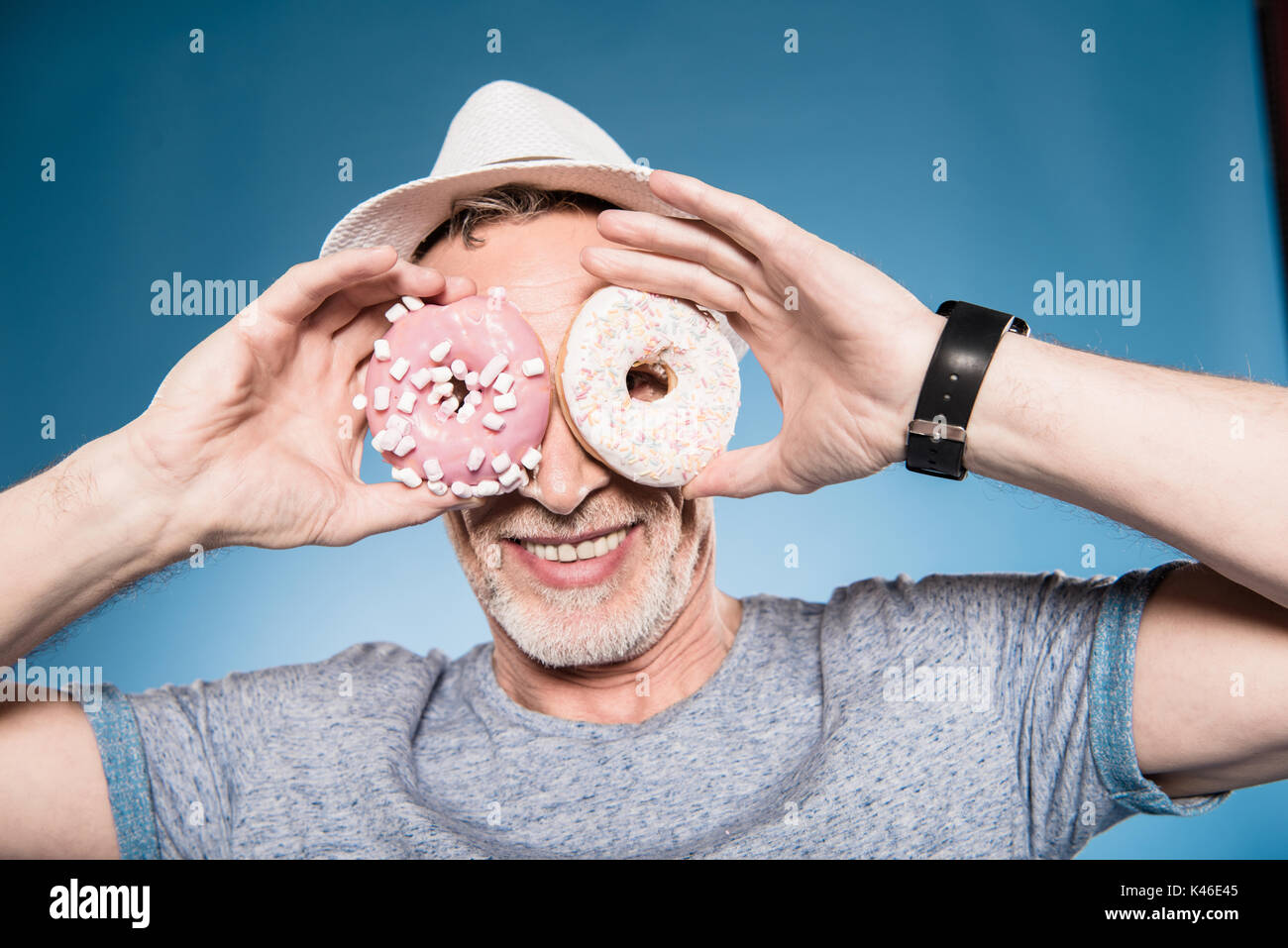 portrait of elderly casual man holding donuts in front of eyes Stock ...