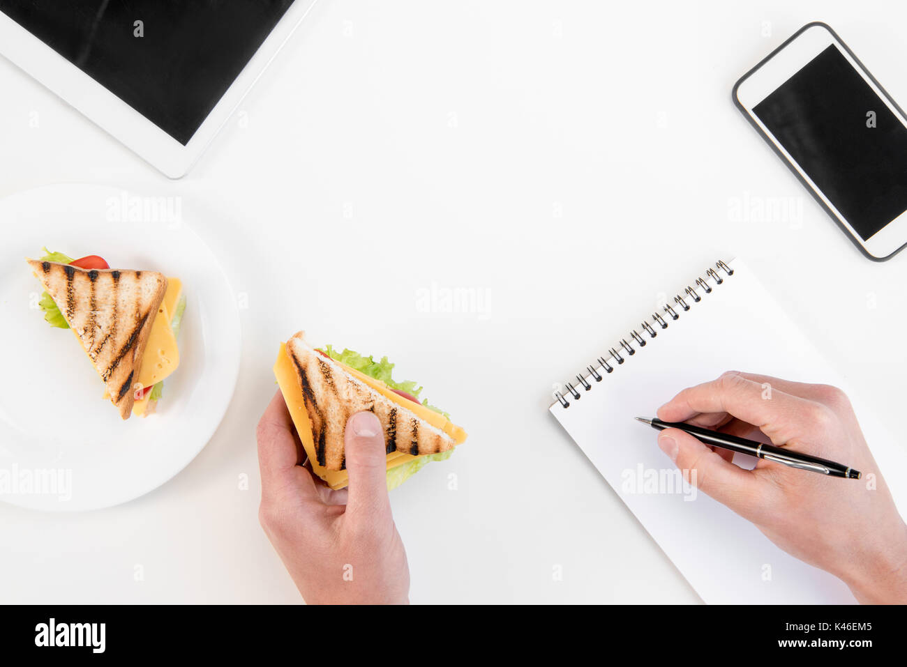Top view of person writing in notebook while eating sandwiches at ...