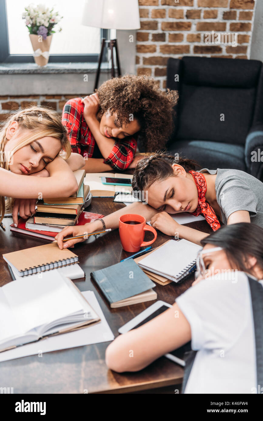 Tired young students sleeping on table with notebooks and digital ...