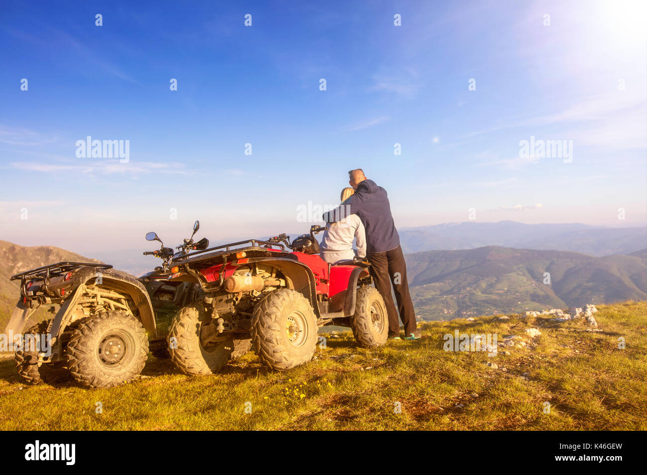 Rear view of young pair near atv. Man is showing something in distance ...