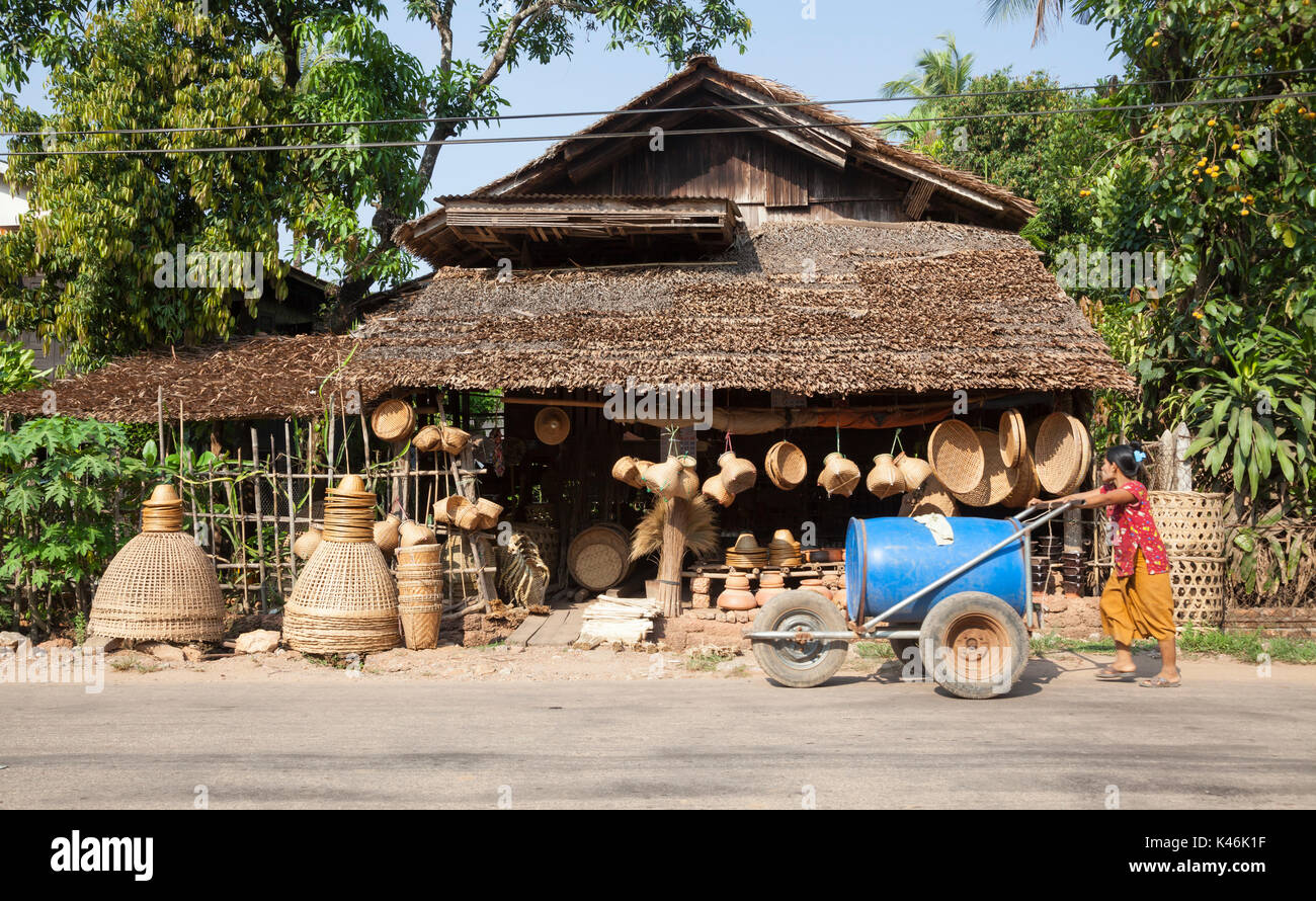 Woman worker pushes water cart past village basket shop in rural ...