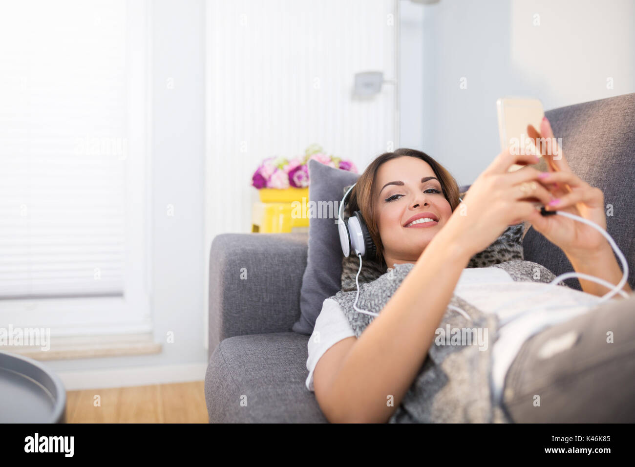 Portrait of happy beautiful woman relaxing on couch listening music ...