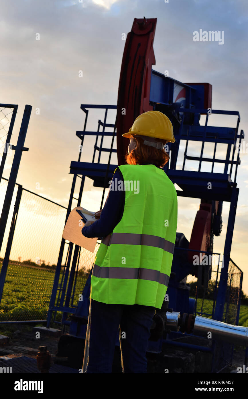 A female petroleum engineer at work on an oil well during dusk time ...