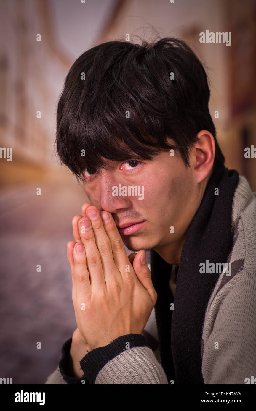 Portrait of a homeless young man in the streets, praying for food in a ...