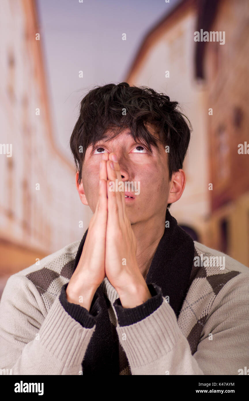Portrait of a homeless young man in the streets, praying to god for ...