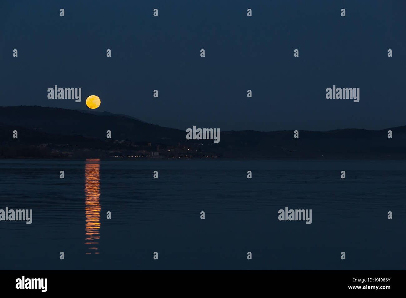 Full moon rising over some hills on a lake, perfectly reflecting on ...