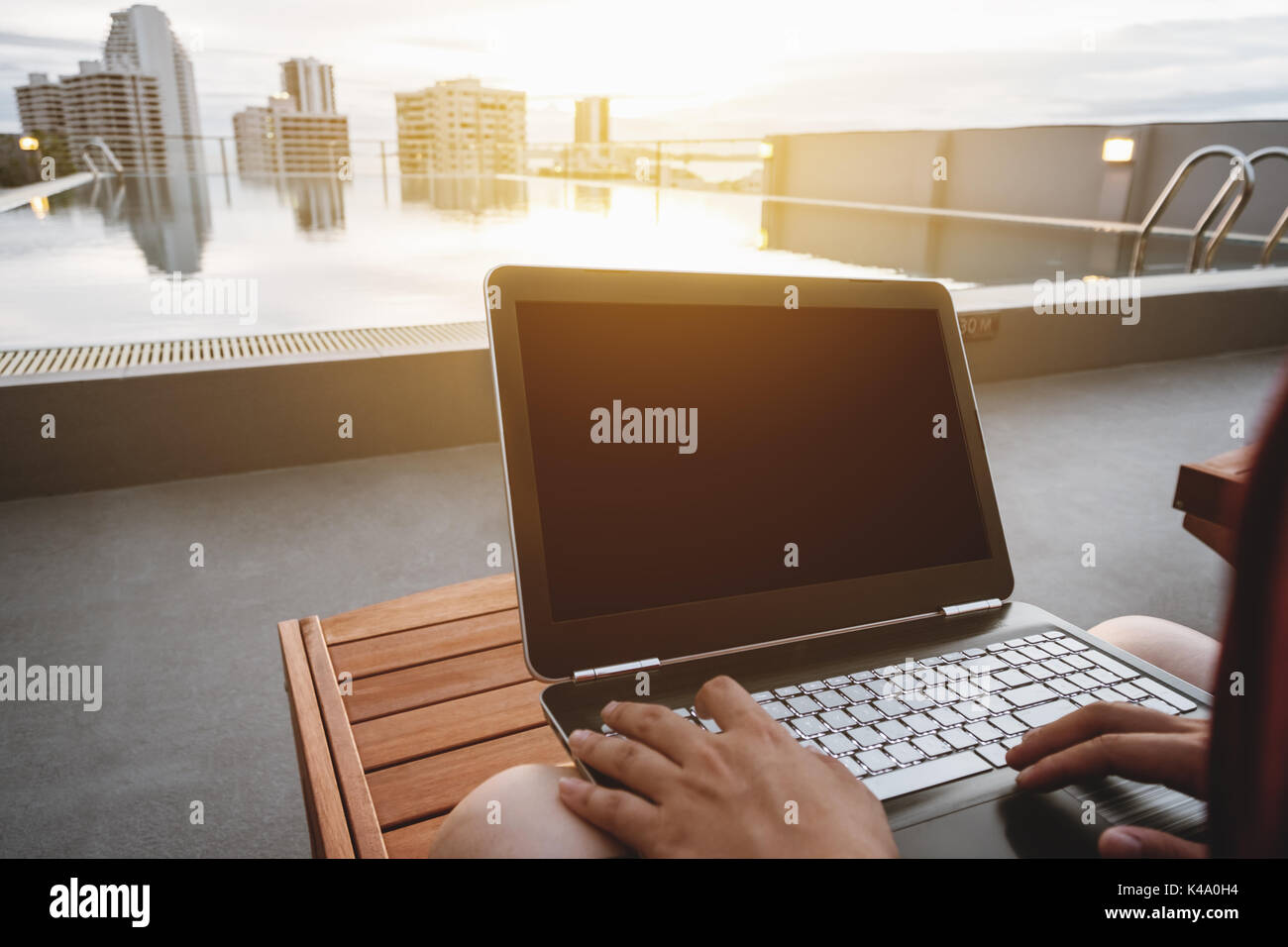 a man using computer laptop, on sunbathe lounge chair at swimming pool ...