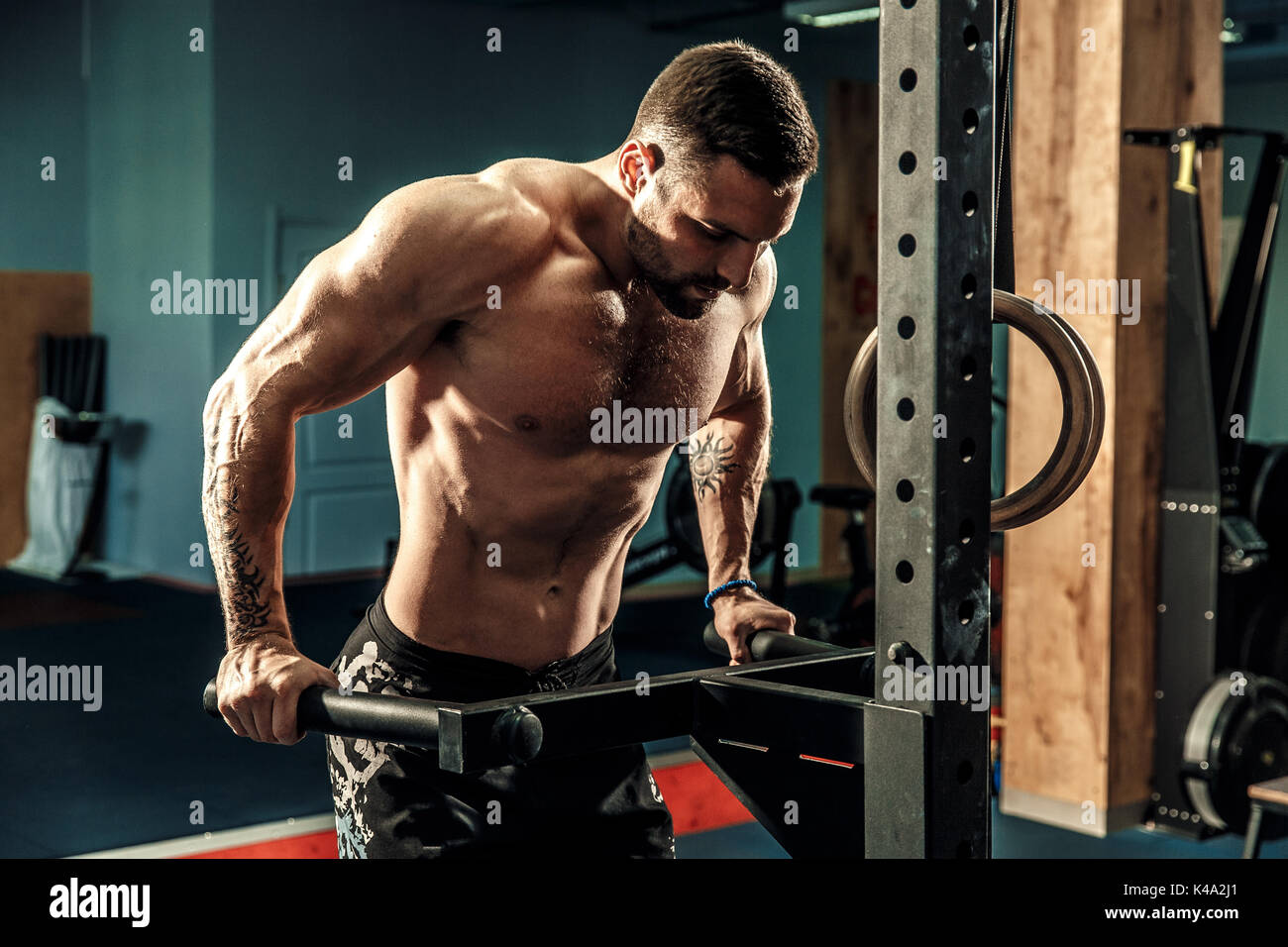 Strong muscular man doing push-ups on uneven bars in crossfit gym Stock ...
