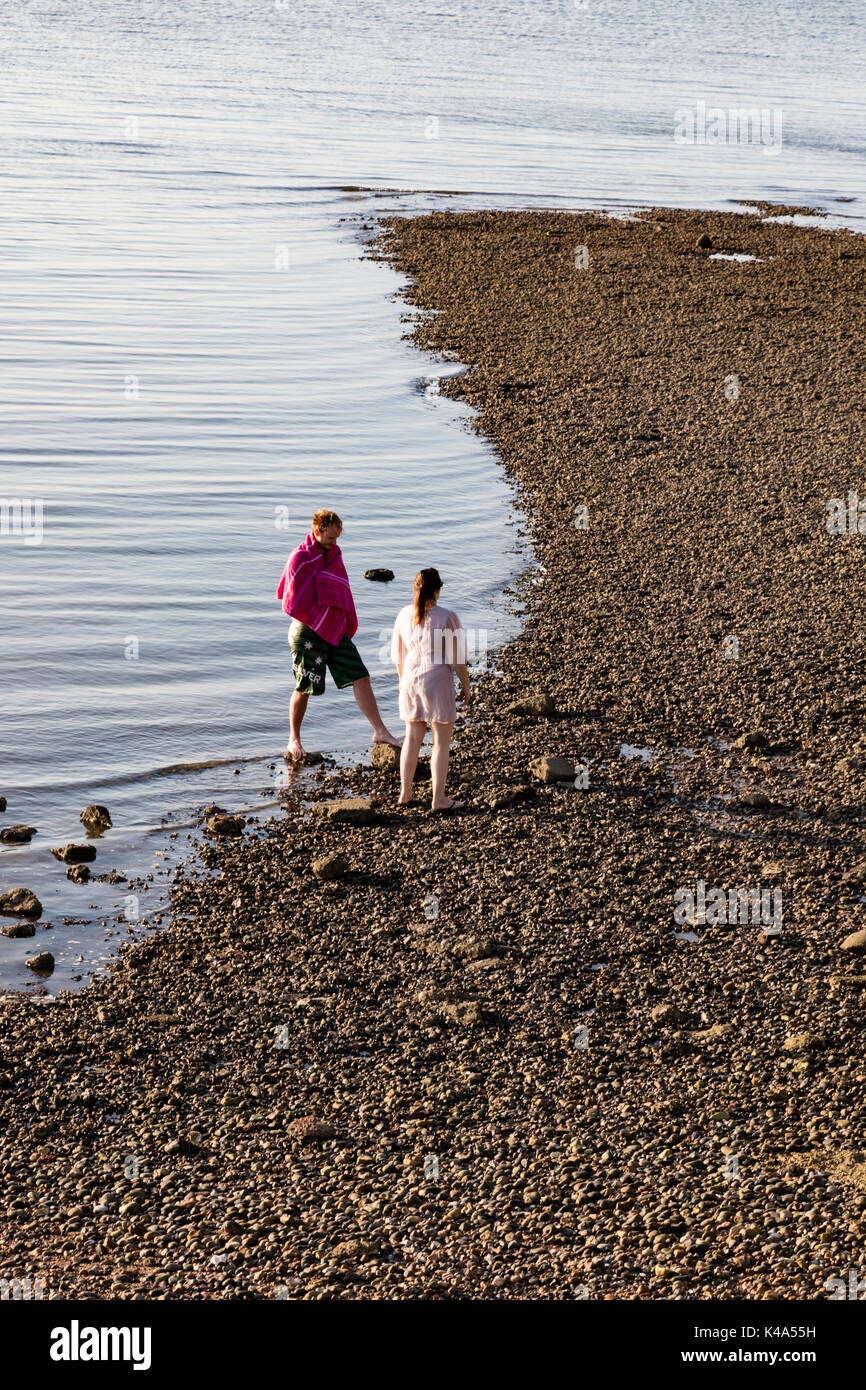 A couple stand and talk in the waters edge in the warm evening light at ...