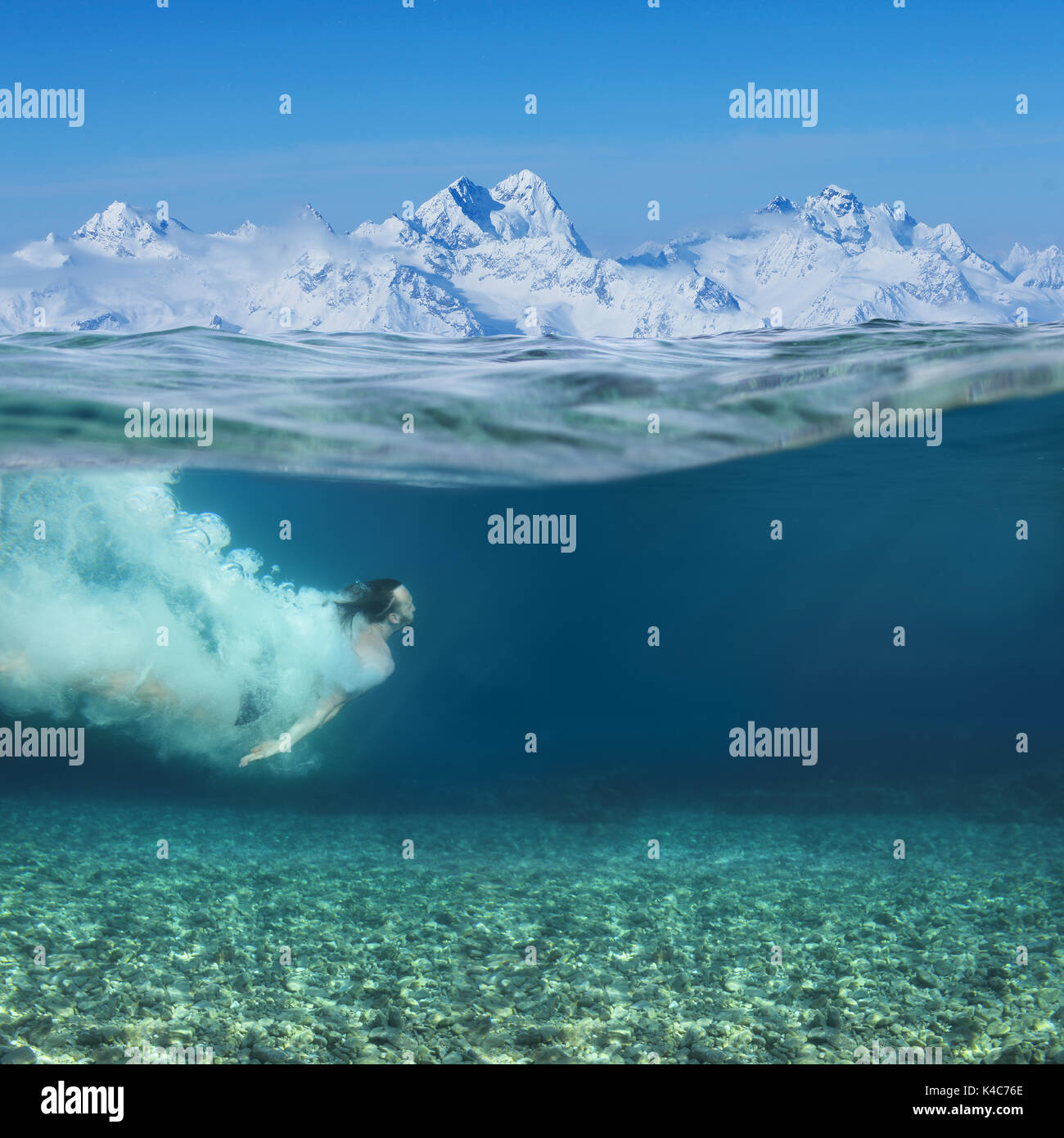 Man swimming underwater in blue transparent sea water, snow mountains ...