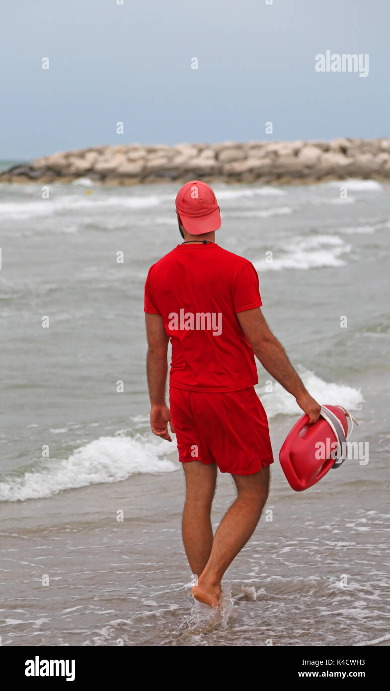 Muscular Lifeguard with red uniform checks the bathers with the rugged ...