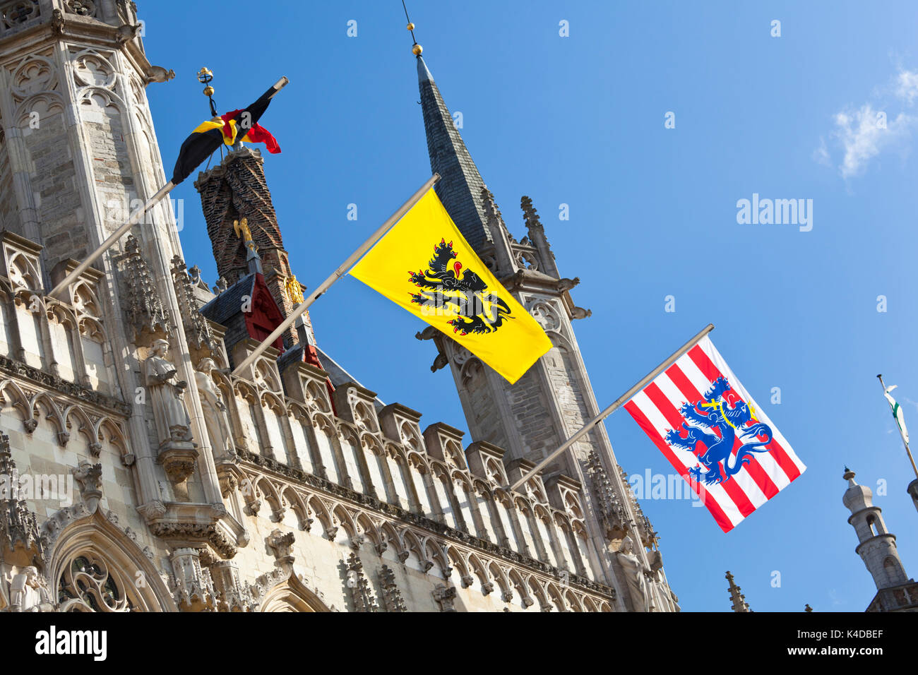The old town hall of Bruges with blue sky and the waving flags of ...