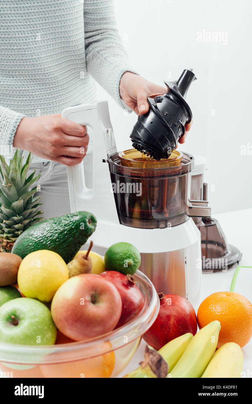 Woman using a juice extractor and preparing healthy drinks using fresh ...