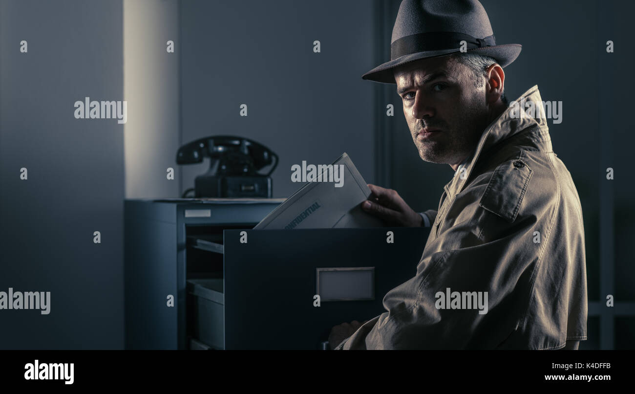 Vintage undercover spy stealing files in a filing cabinet late at night ...