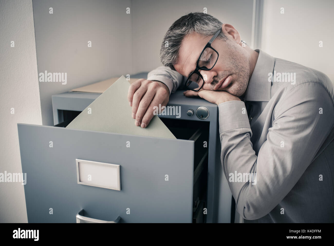 Tired lazy office worker leaning on a filing cabinet and sleeping, he ...