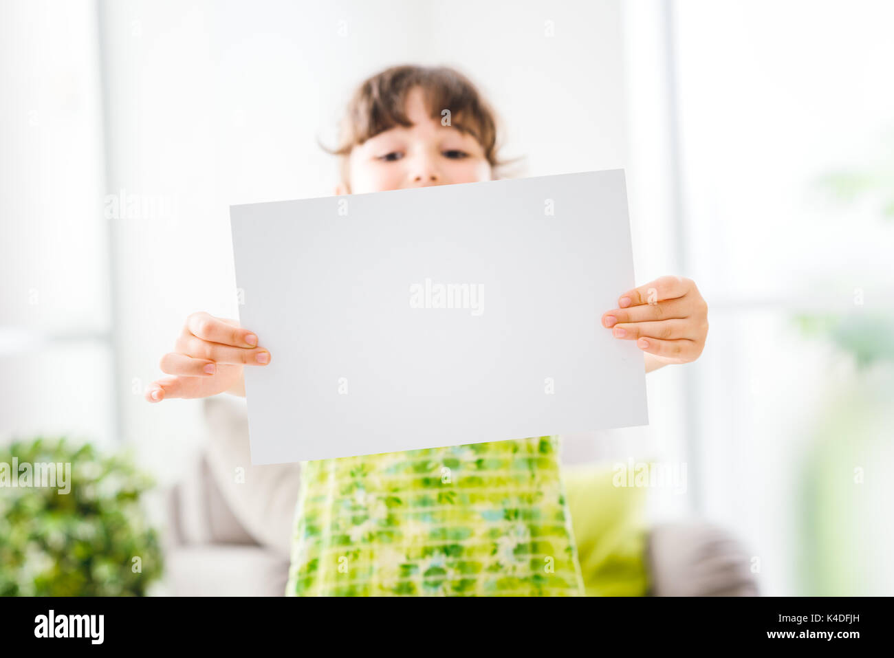 Cute young girl peeking behind a blank sign, room interior on the ...
