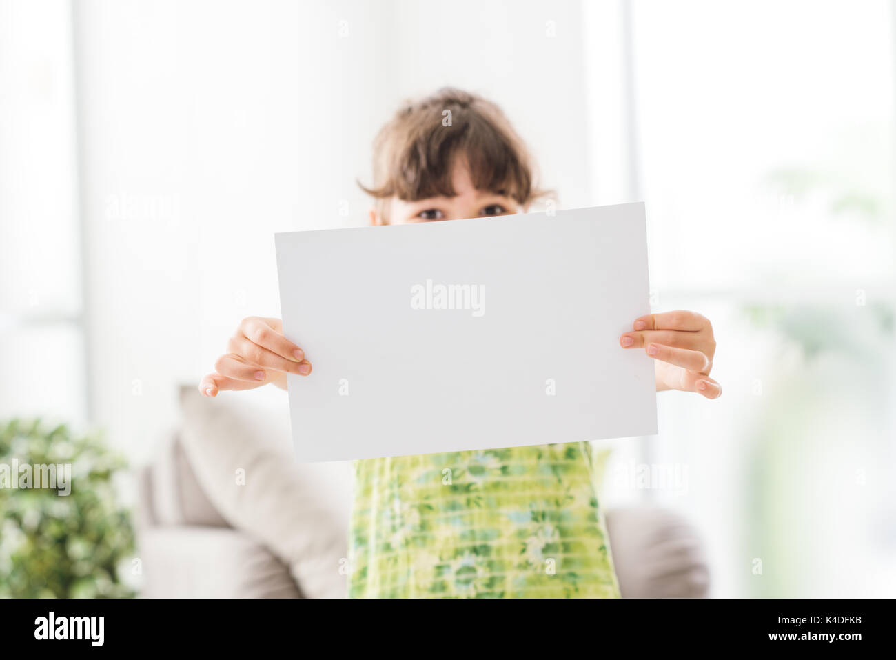 Cute young girl peeking behind a blank sign, room interior on the ...