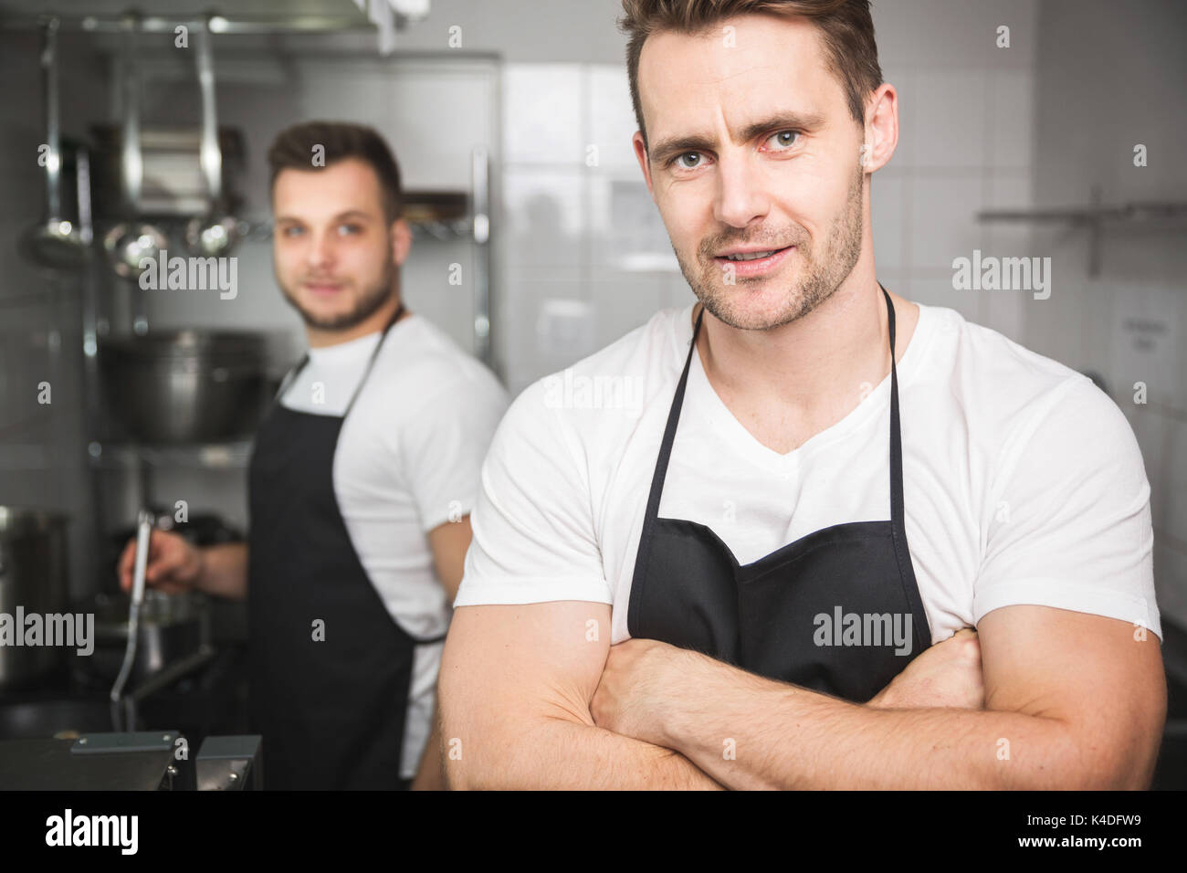 Front portrait of male chef with crossed arms and his coworker in ...