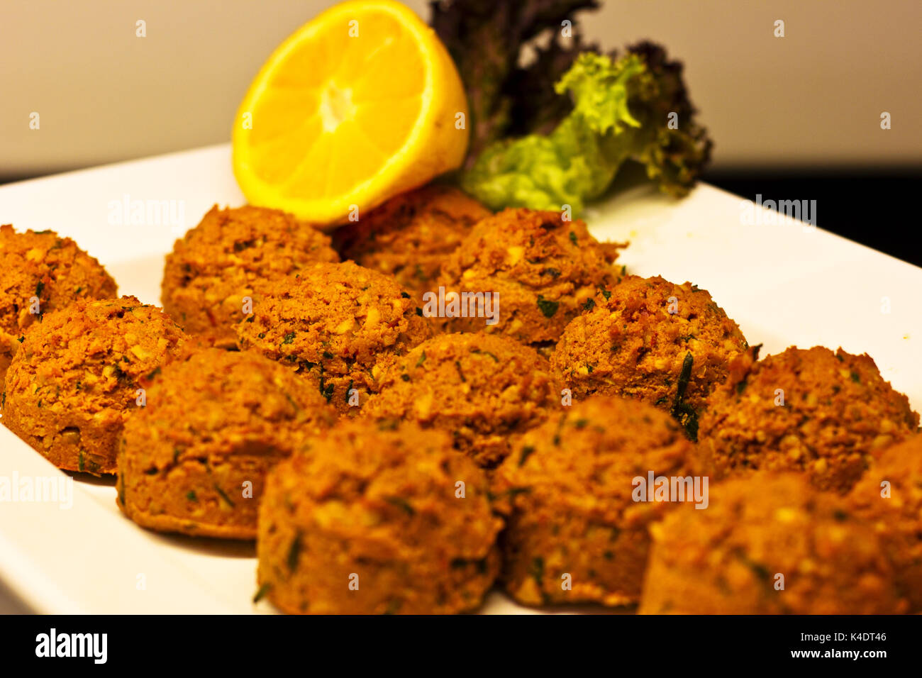 Cold appetizer of red lentils balls with lemon and greens in back side ...