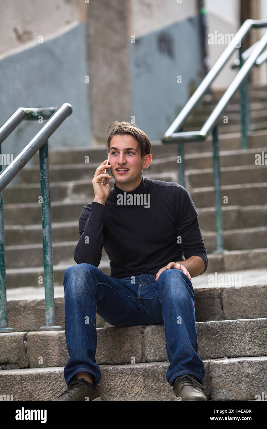 Young man talking on mobile while sitting on outdoor stone steps Stock ...