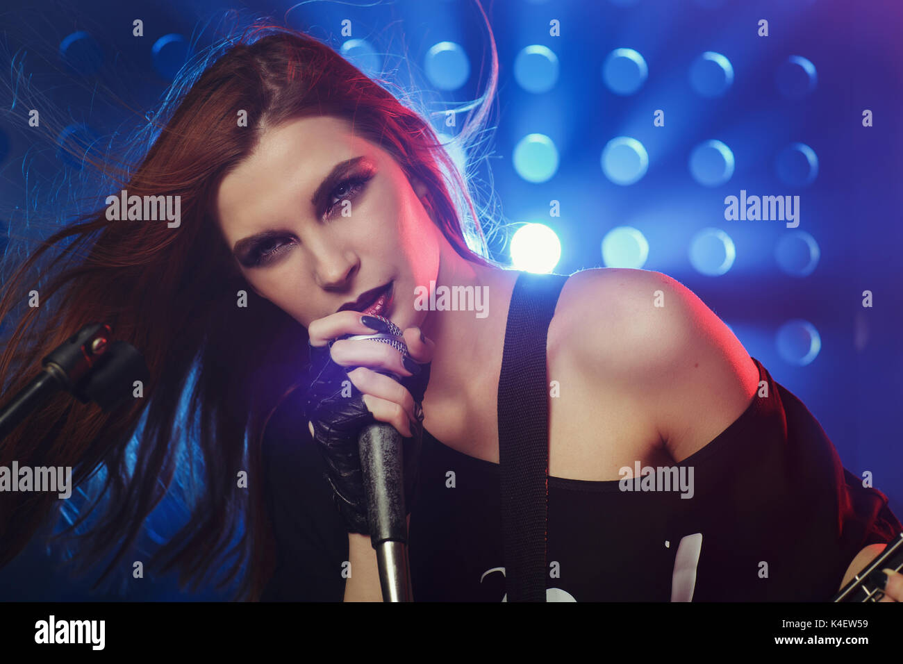 Beautiful girl with a microphone and a guitar in hand on stage singing ...