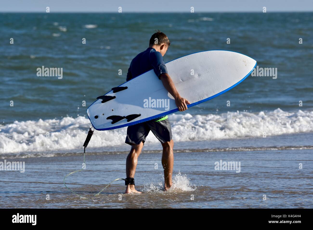 Surfer walking down beach while carrying surfboard Stock Photo - Alamy