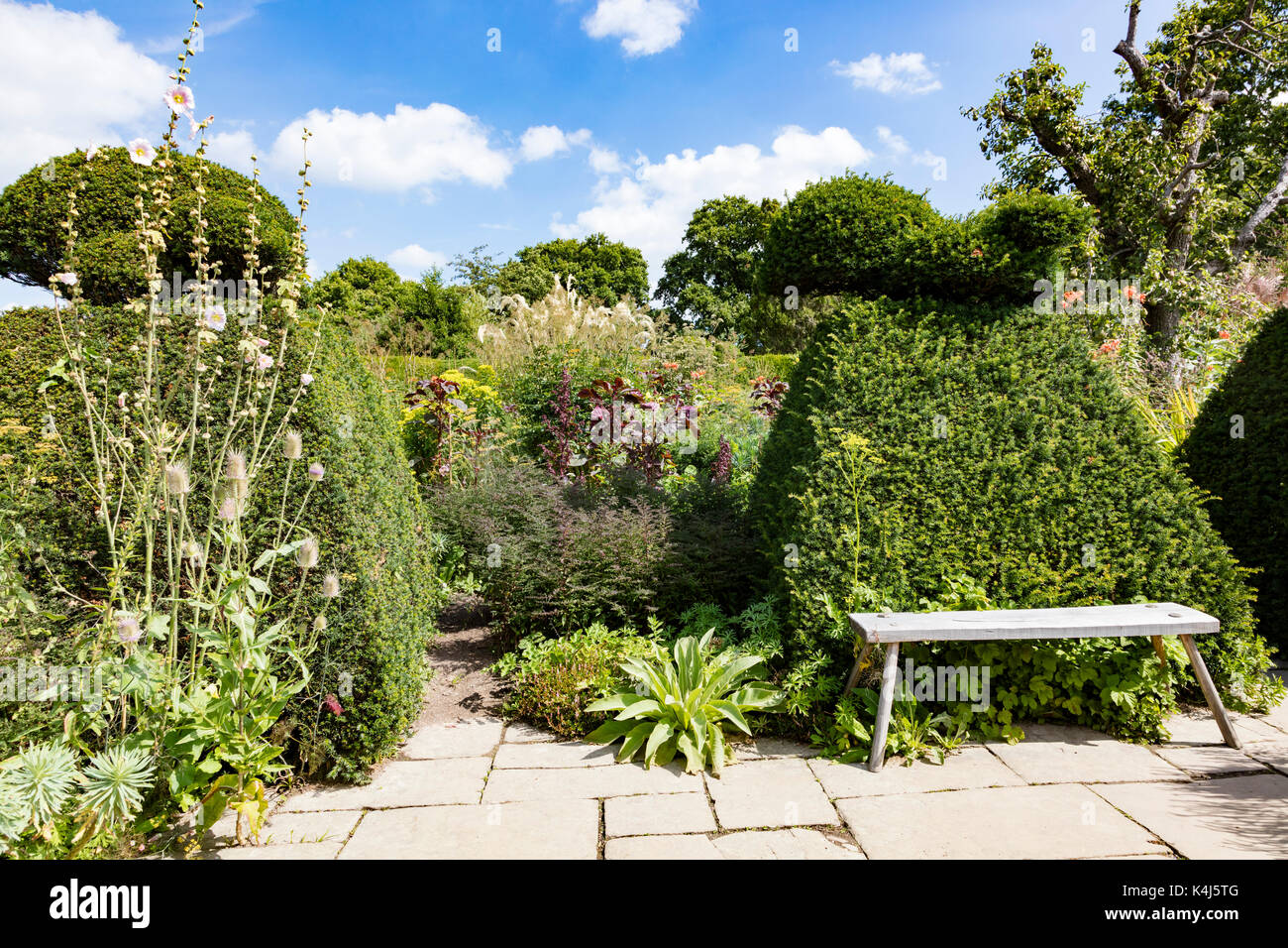 A garden bench provides a quiet spot amongst the beds and topiary for ...