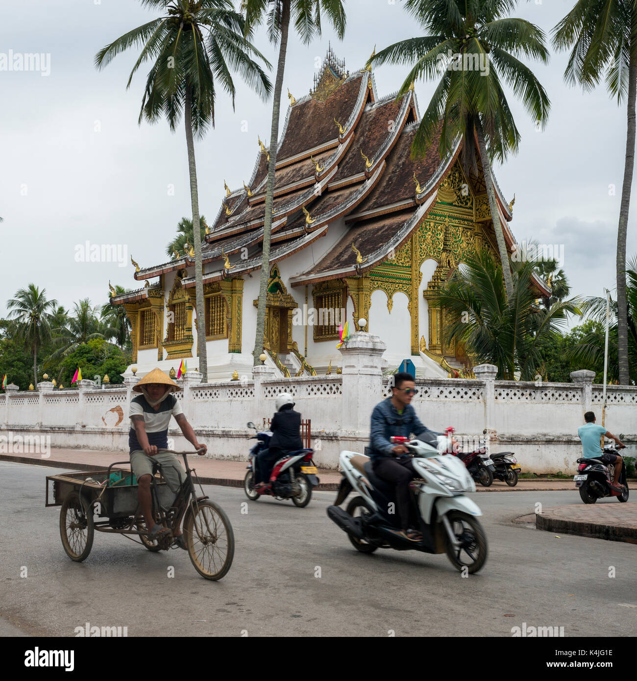People riding vehicles on road with Royal Temple in background, Haw Pha ...