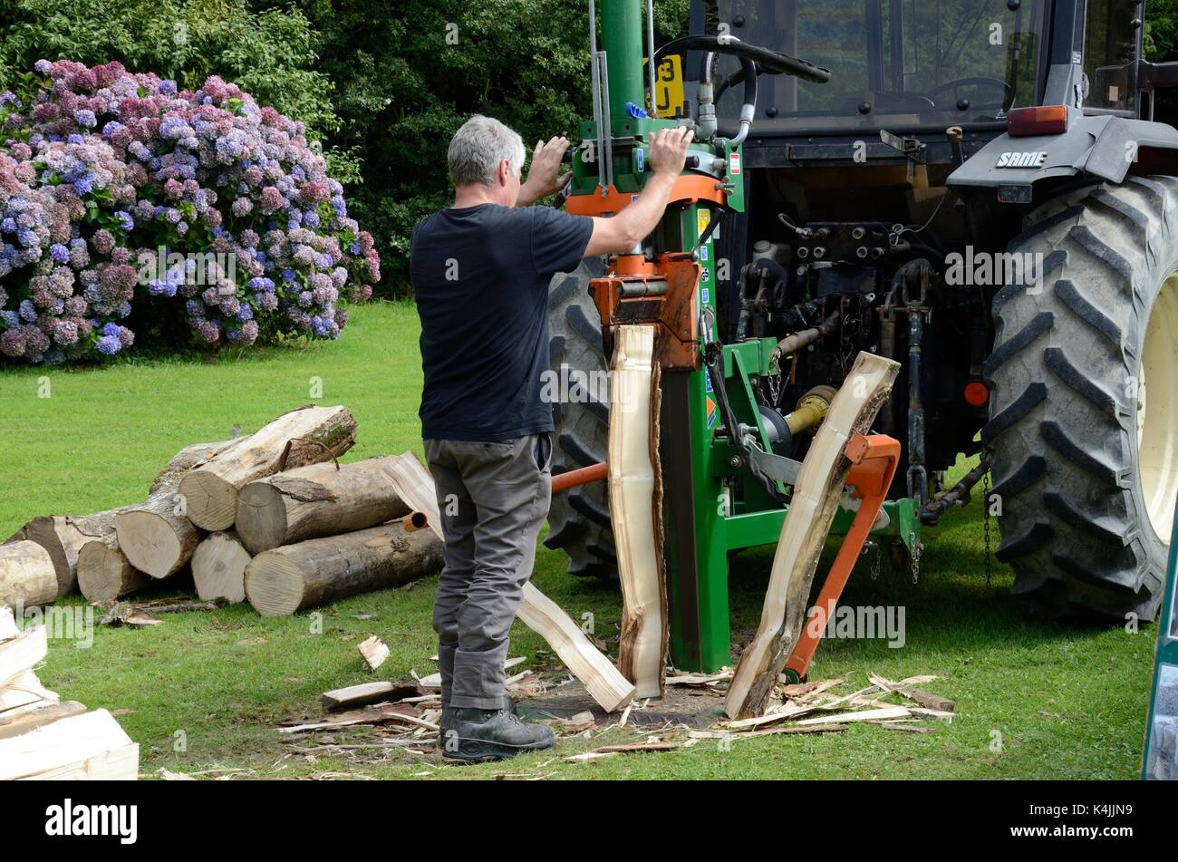 A man using a log splitter machine on the back of a tractor Stock Photo ...