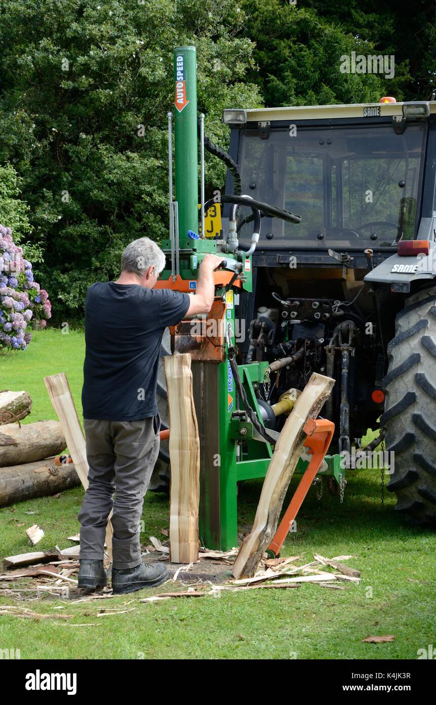 A man using a log splitter machine on the back of a tractor Stock Photo ...