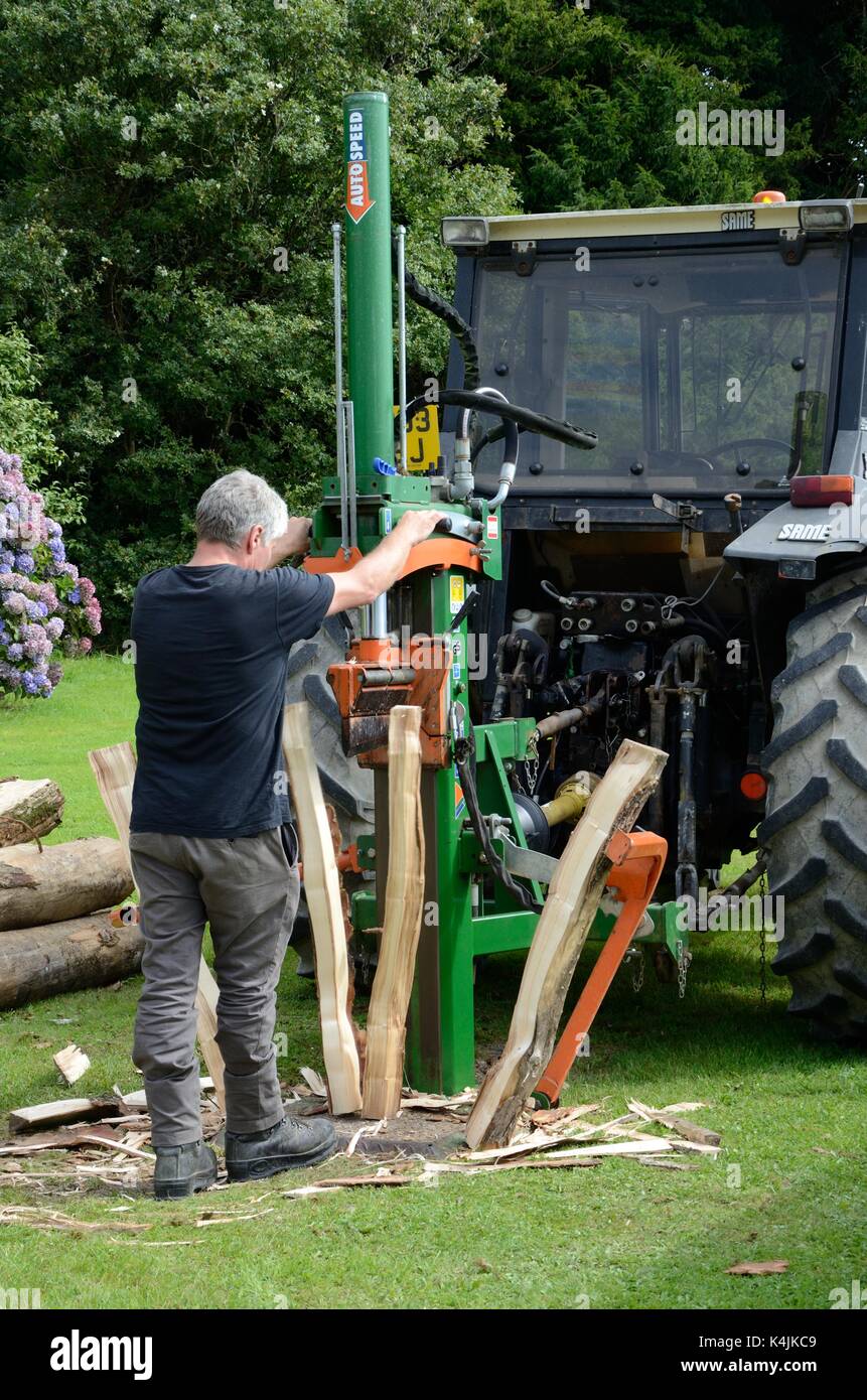 A man using a log splitter machine on the back of a tractor Stock Photo ...