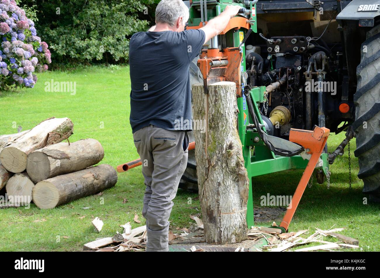 A man using a log splitter machine on the back of a tractor Stock Photo ...