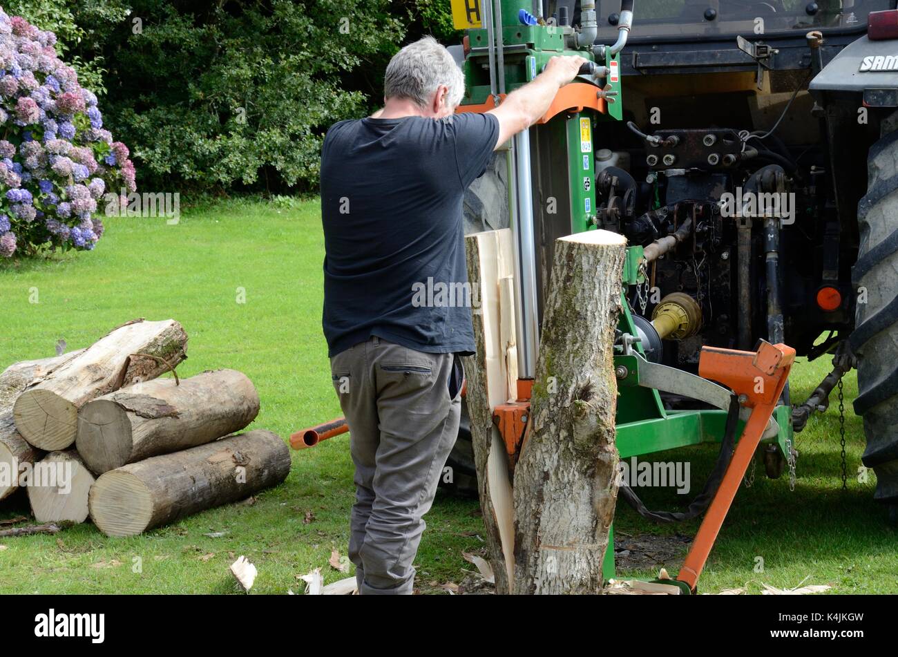 A man using a log splitter machine on the back of a tractor Stock Photo ...