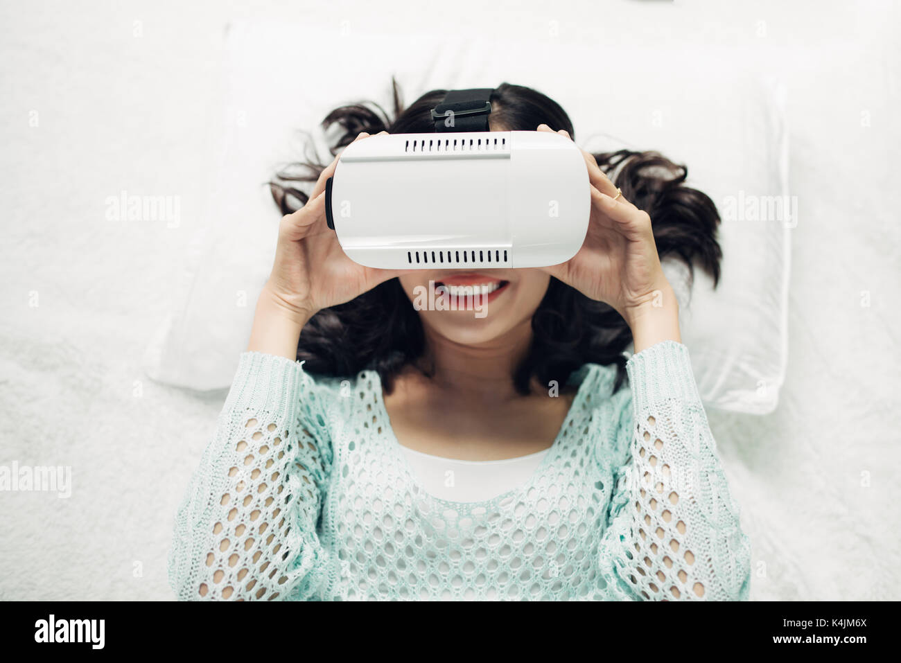 Asian woman wearing vr goggles lying on bed Stock Photo - Alamy