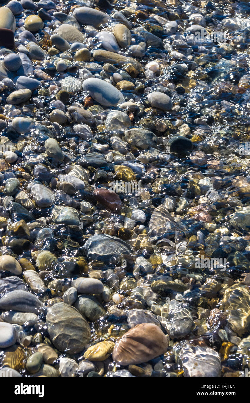 sea pebble beach with multicoloured stones, transparent waves with foam ...