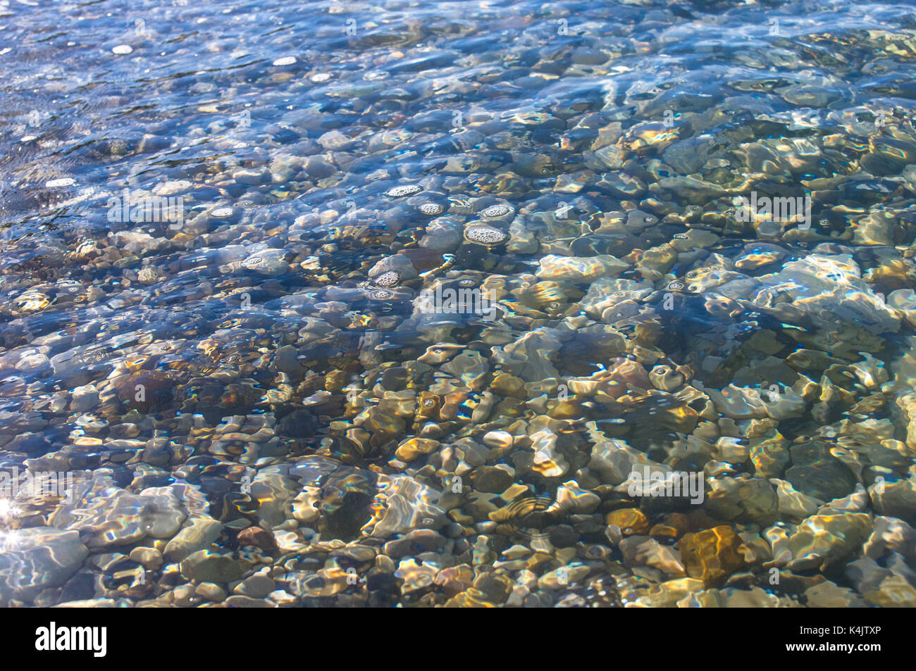 sea pebble beach with multicoloured stones, transparent waves with foam ...