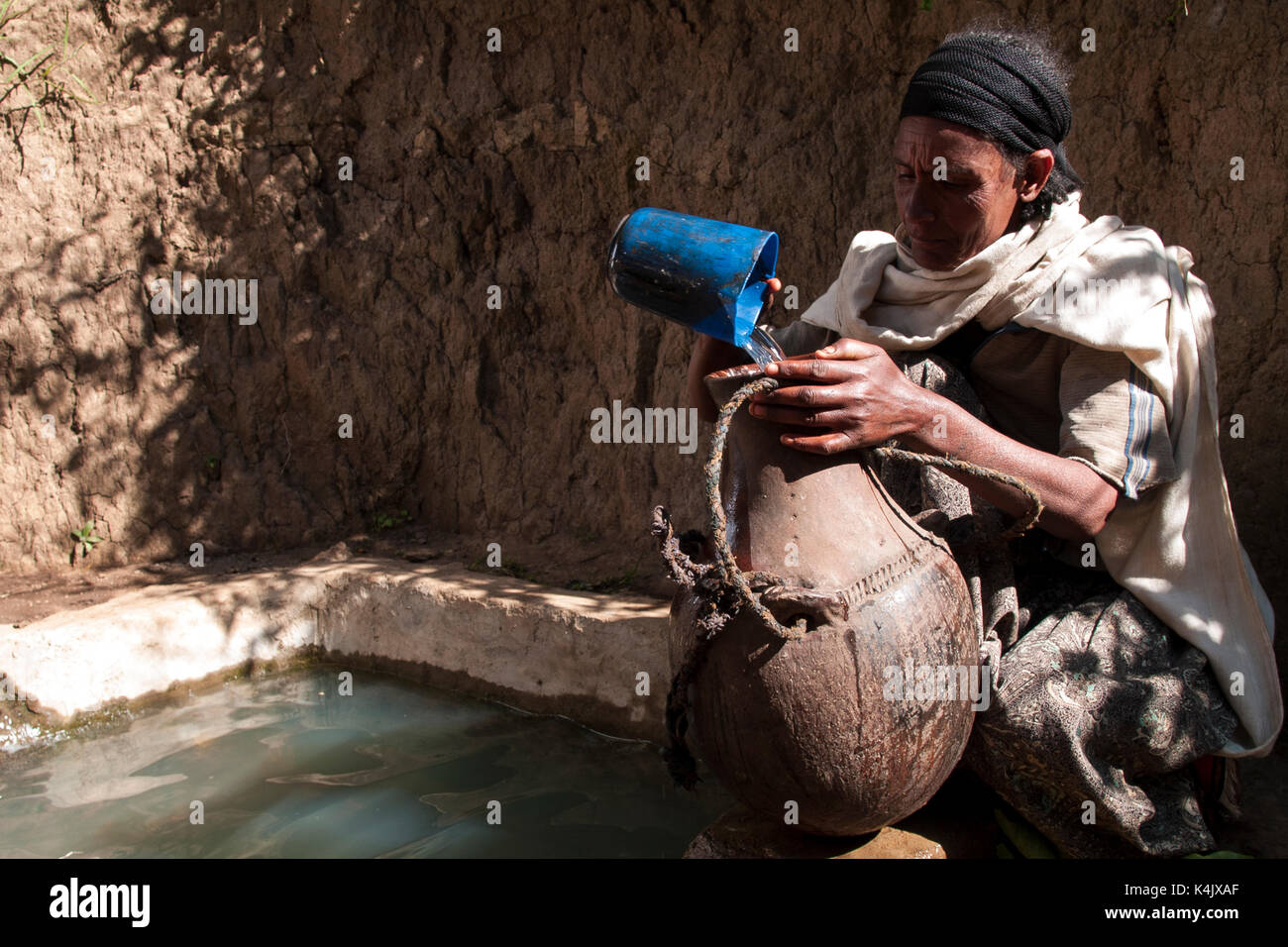 A woman fills a traditional water pot from a capped spring, Ethiopia ...