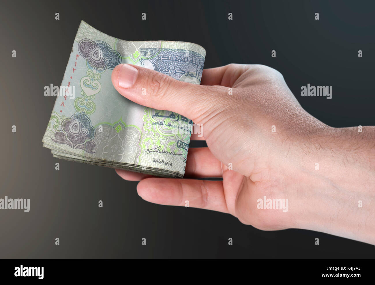 A male hand handing over a wad of folded dubai dirham bank notes on an ...
