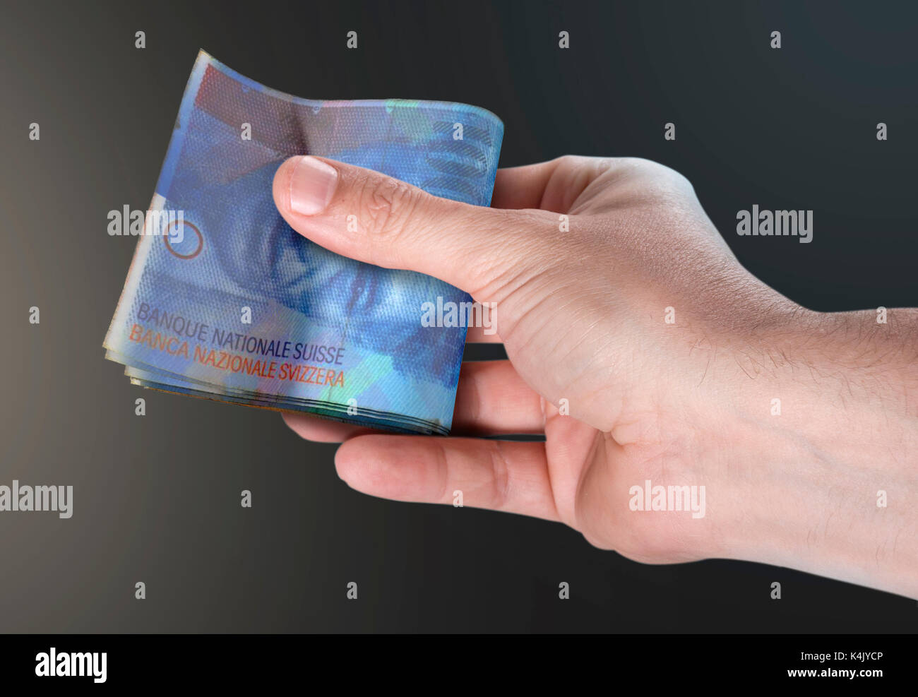 A male hand handing over a wad of folded swiss franc bank notes on an ...