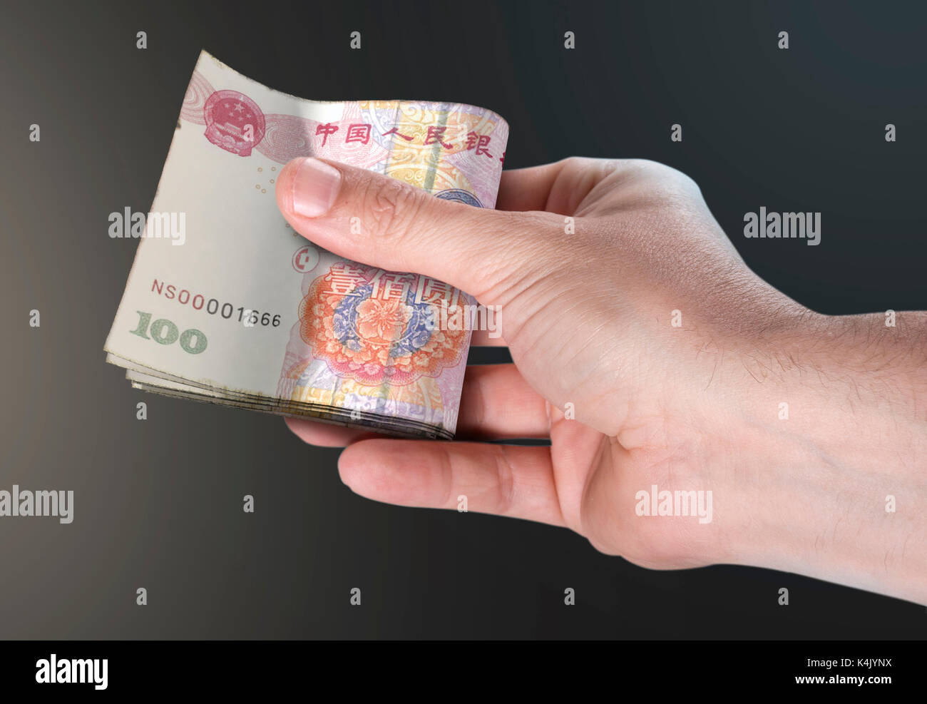 A male hand handing over a wad of chinese yuan folded bank notes on an ...