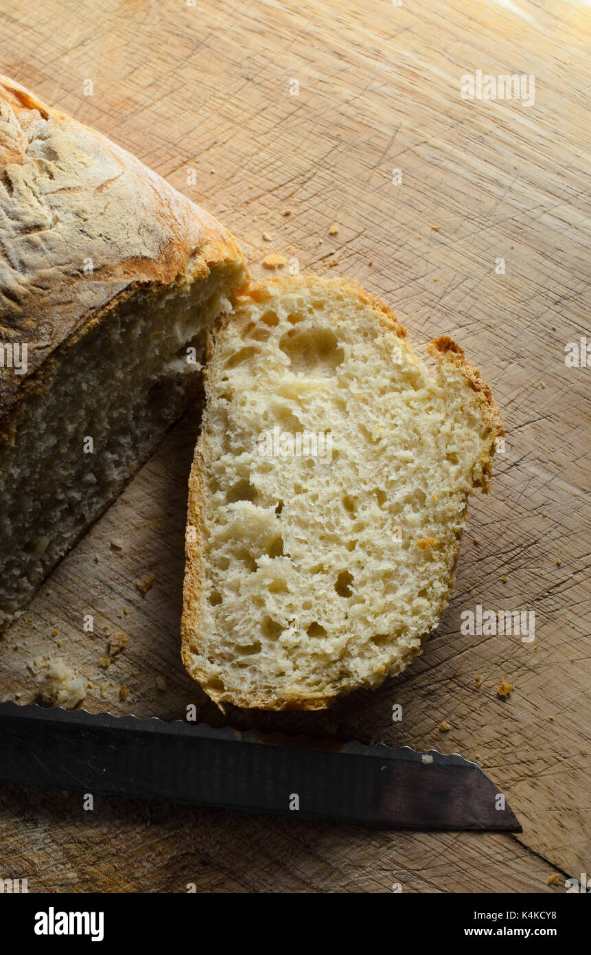 Overhead shot of freshly baked loaf of bread. First slice cut and lying ...