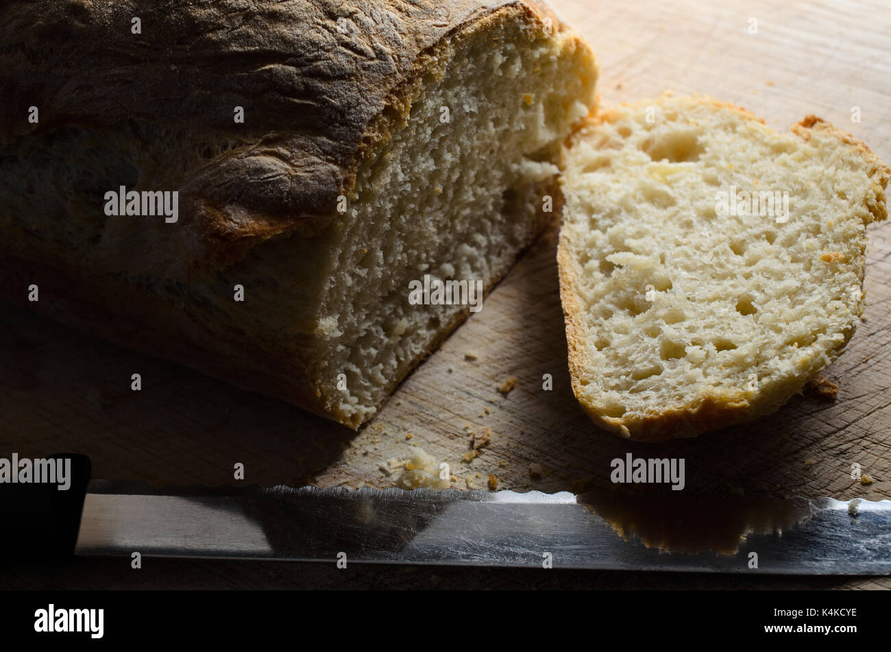 Freshly baked loaf of crusty bread with first slice cut and lying face ...