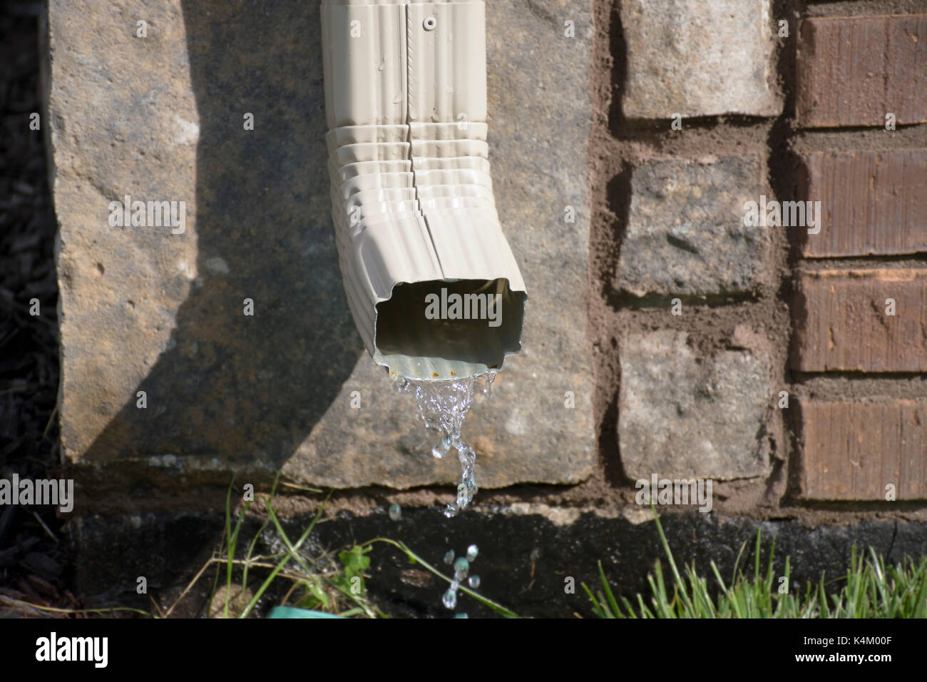 A rain gutter downspout with water coming out, with stones and bricks ...