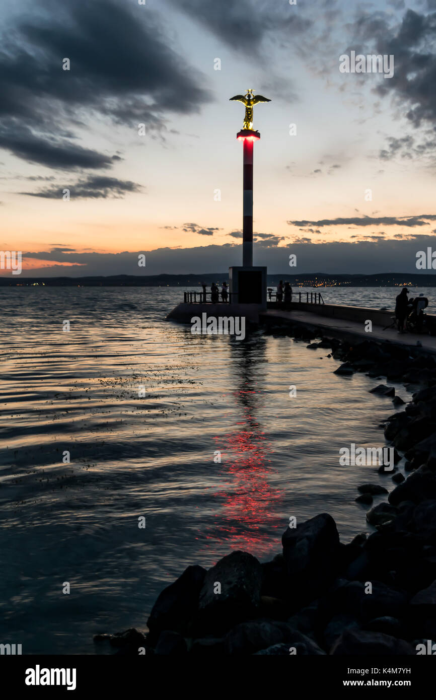 Lighthouse on lake at dusk. Lighthouse, red light reflecting on calm ...